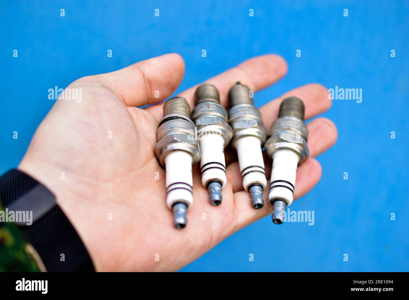 Four white car spark plugs in hand on a blue background Stock Photo - Alamy