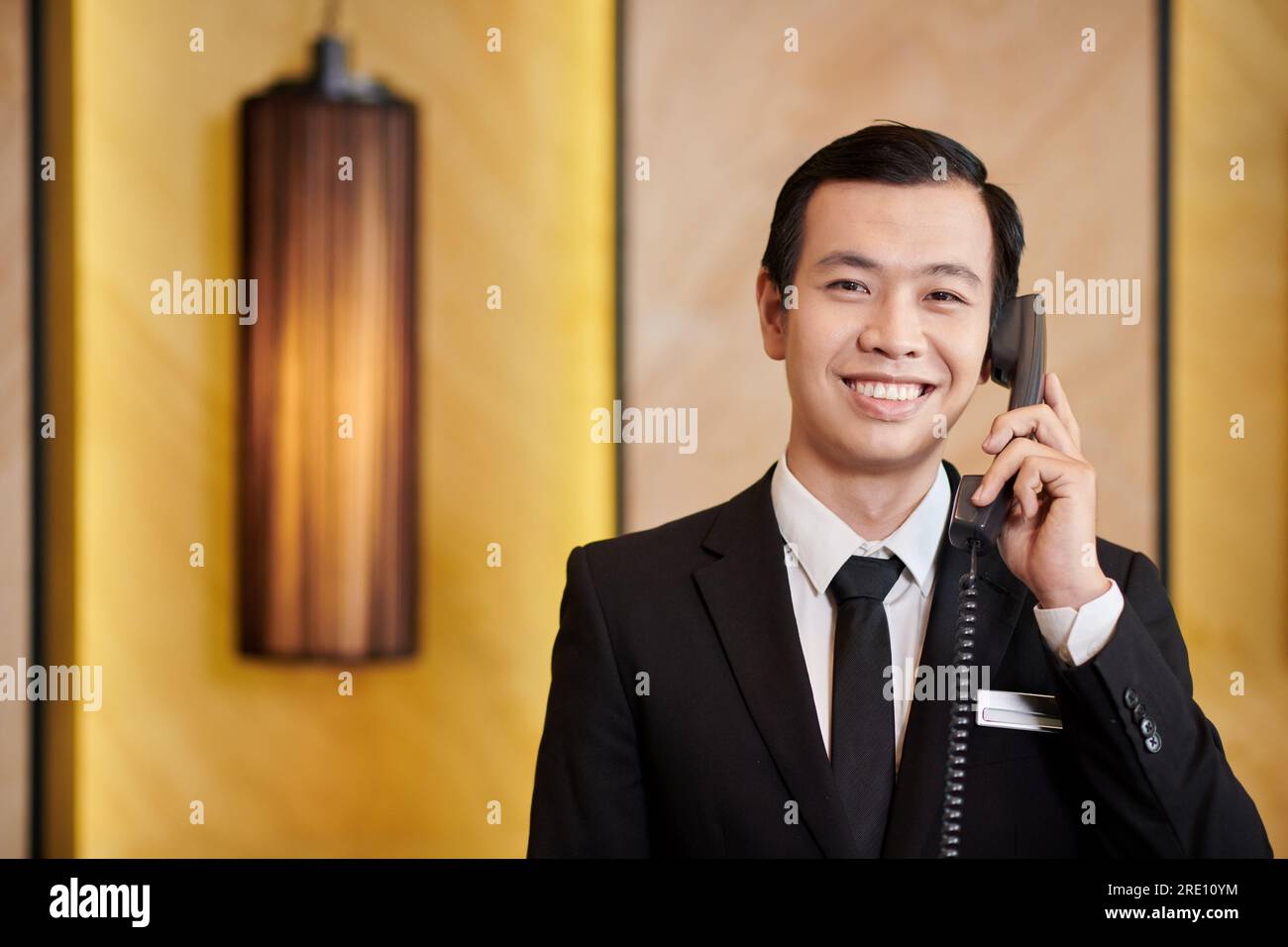 Portrait of positive hotel receptionist talking on phone with guest ...
