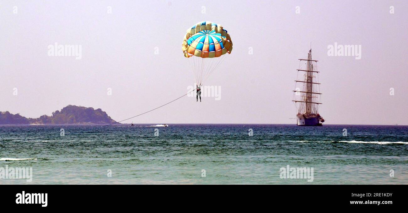 Parasailing above the sea with a pretty sailing boat in the background ...