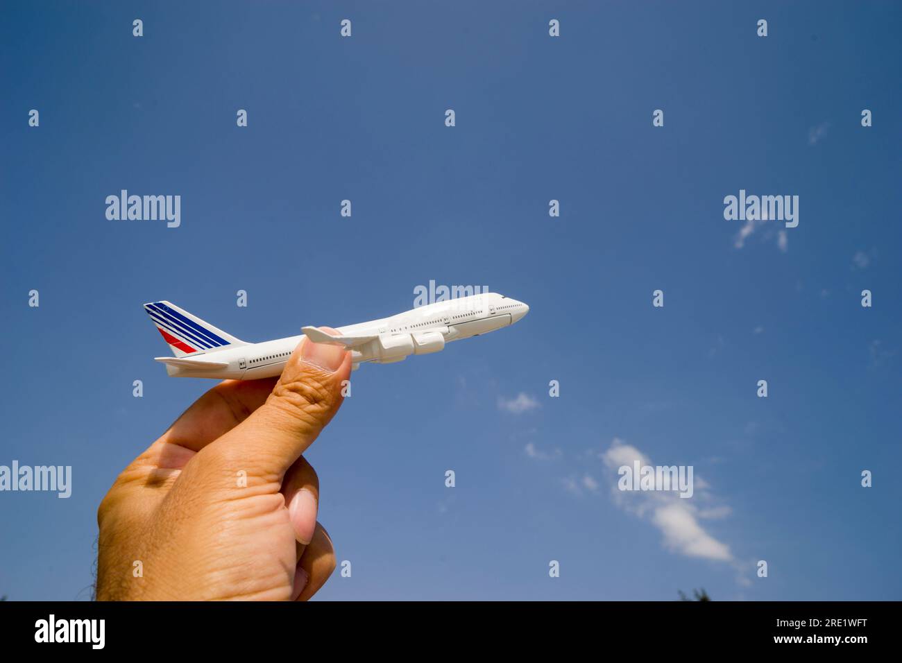 A man's hand holds a model airplane against a blue sky with white ...