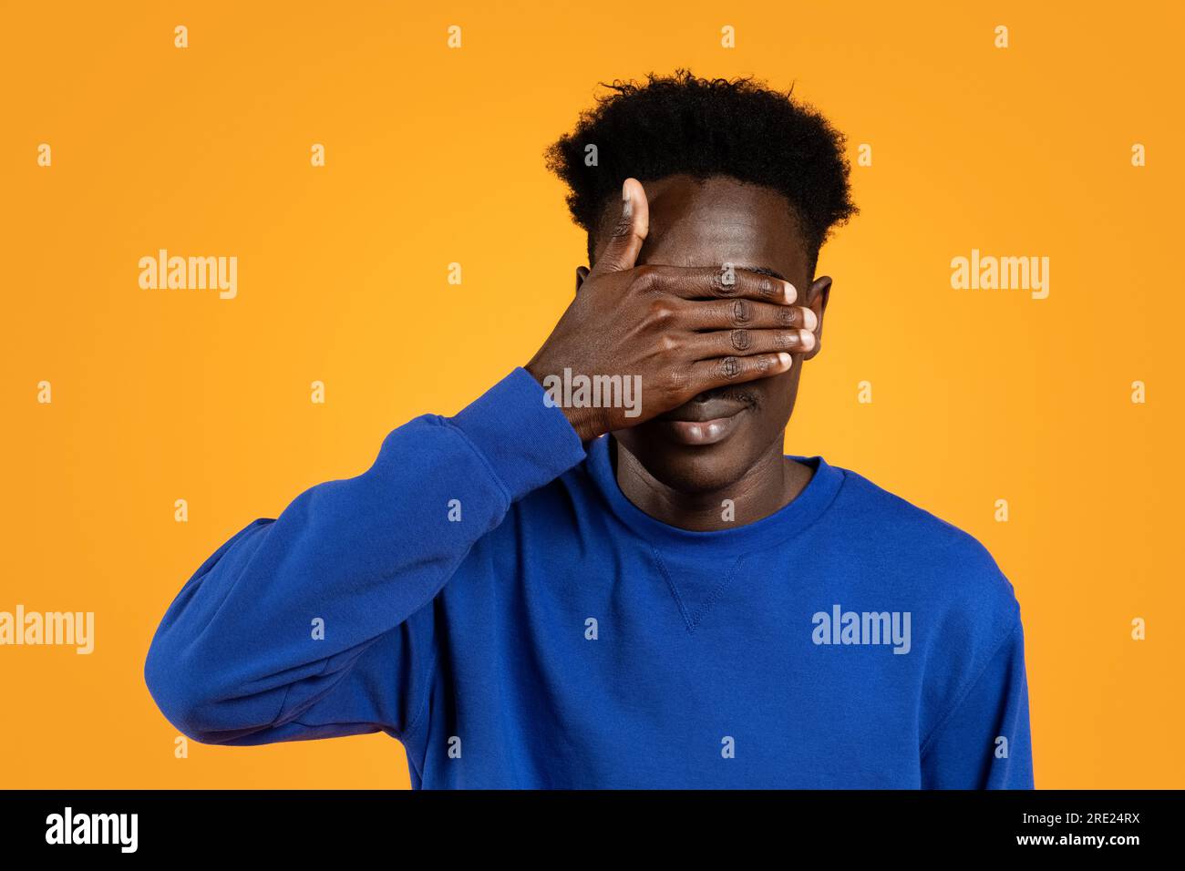 Young black man covering his eyes with palm, yellow background Stock ...