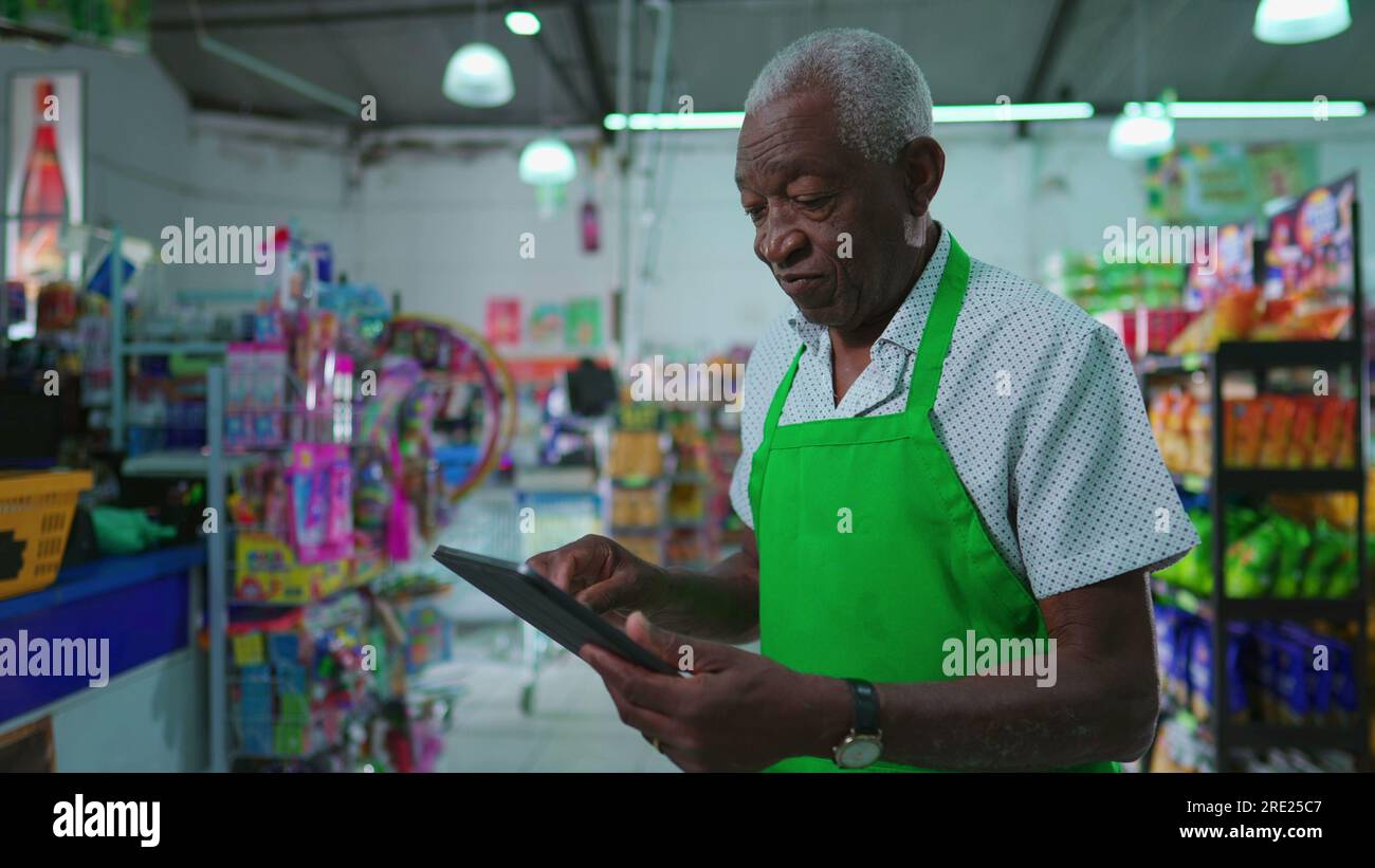 African American senior employee of supermarket using tablet device ...