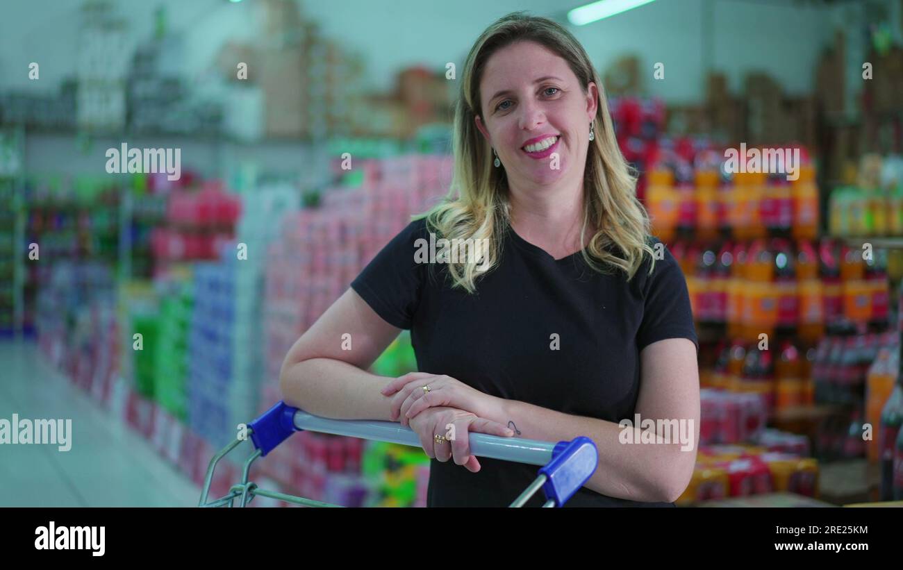 Happy female consumer posing inside supermarket aisle with products in ...