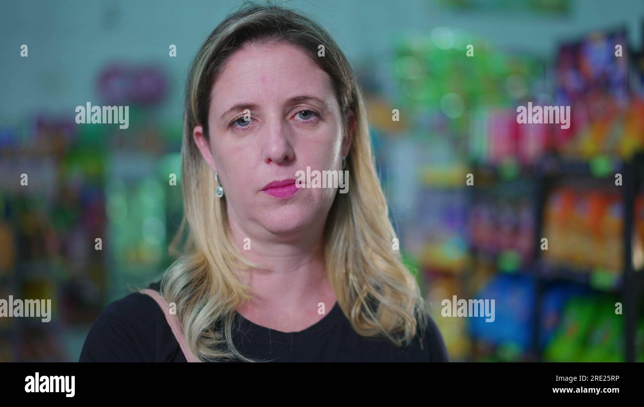 Female consumer standing in supermarket holding basket with serious ...