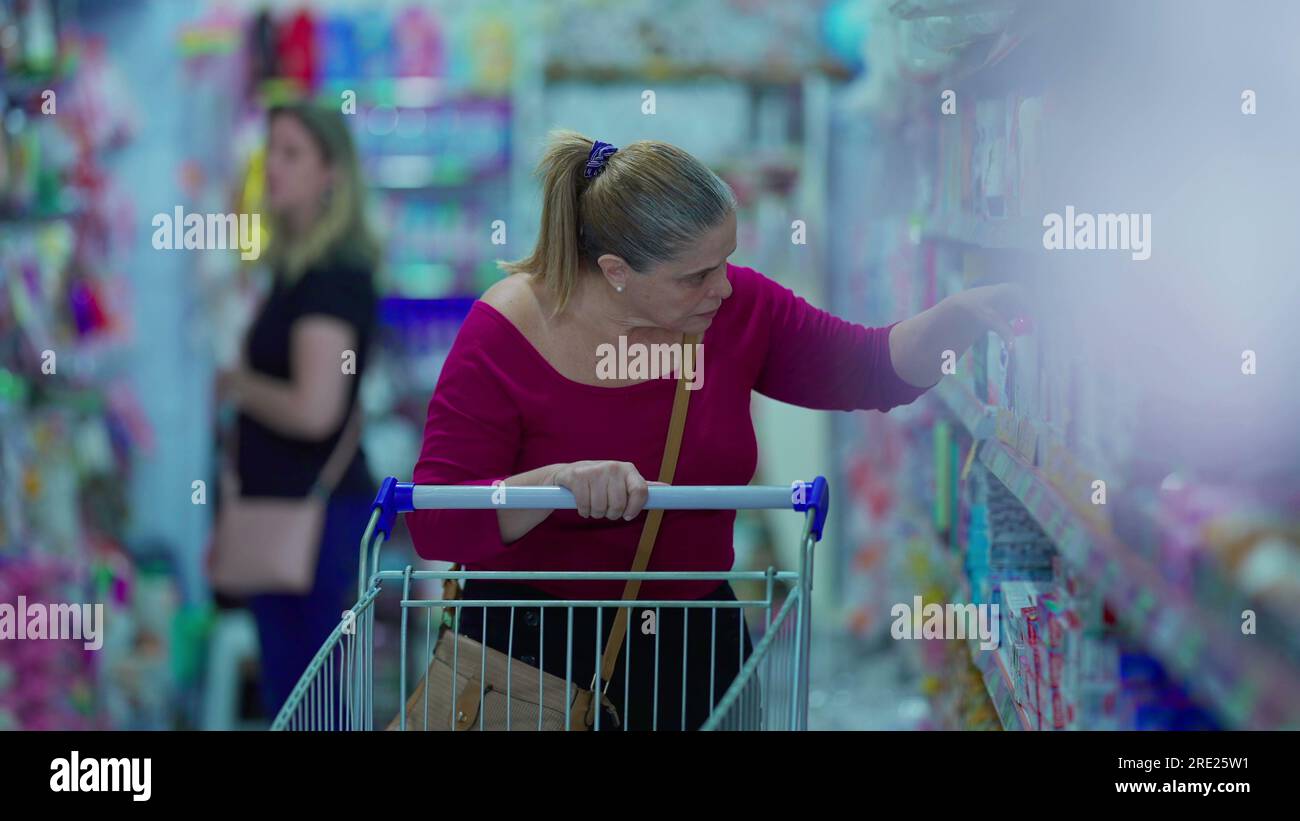 Female grocery shopper walking in aisle browsing for products on shelf ...