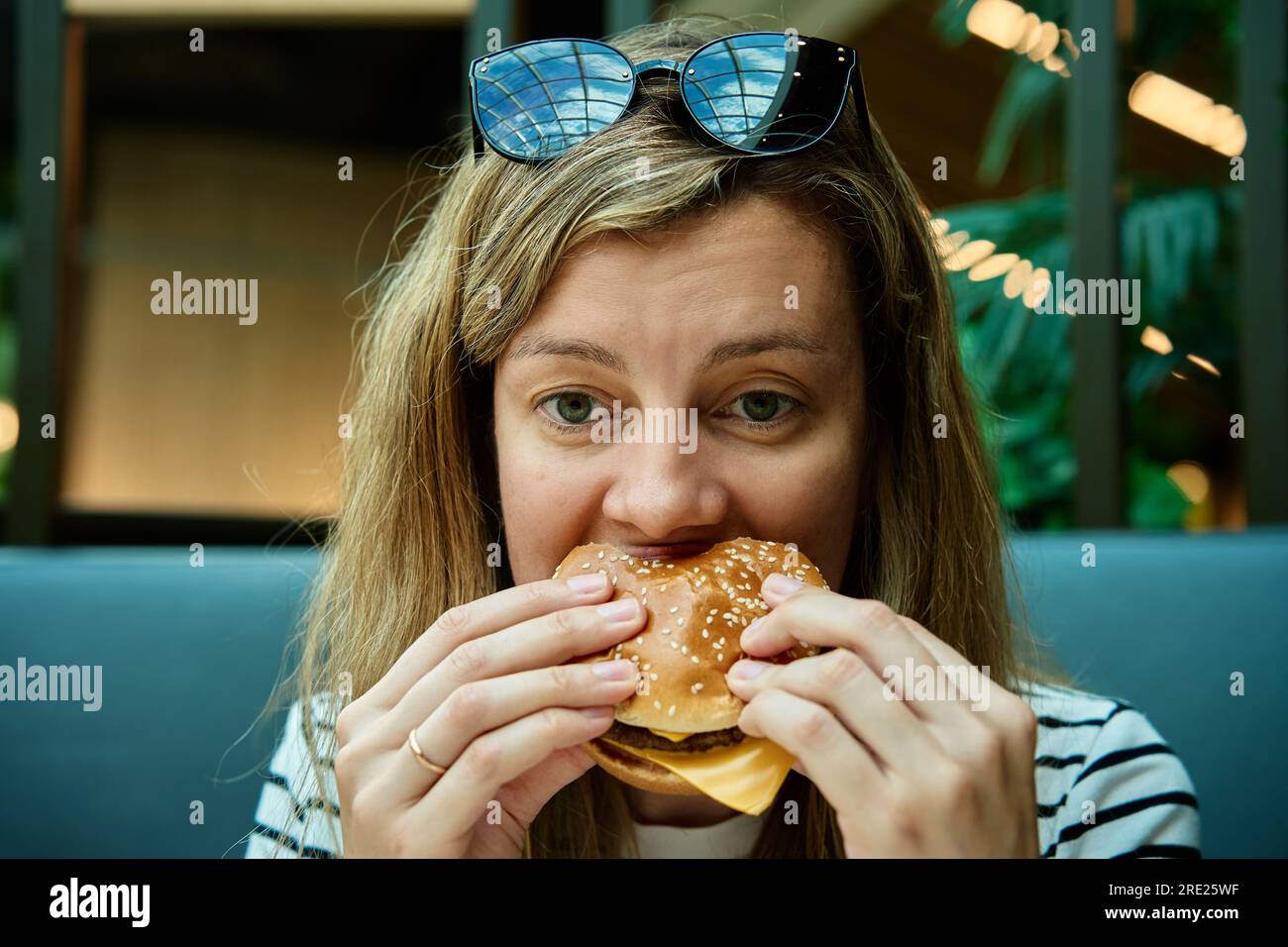 Woman eating burger in restaurant. Close up shot of female biting ...