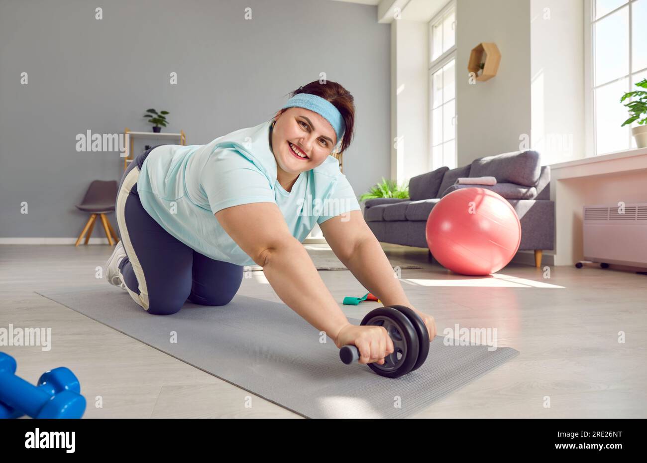Happy, overweight woman doing fitness exercise with ab roller during ...