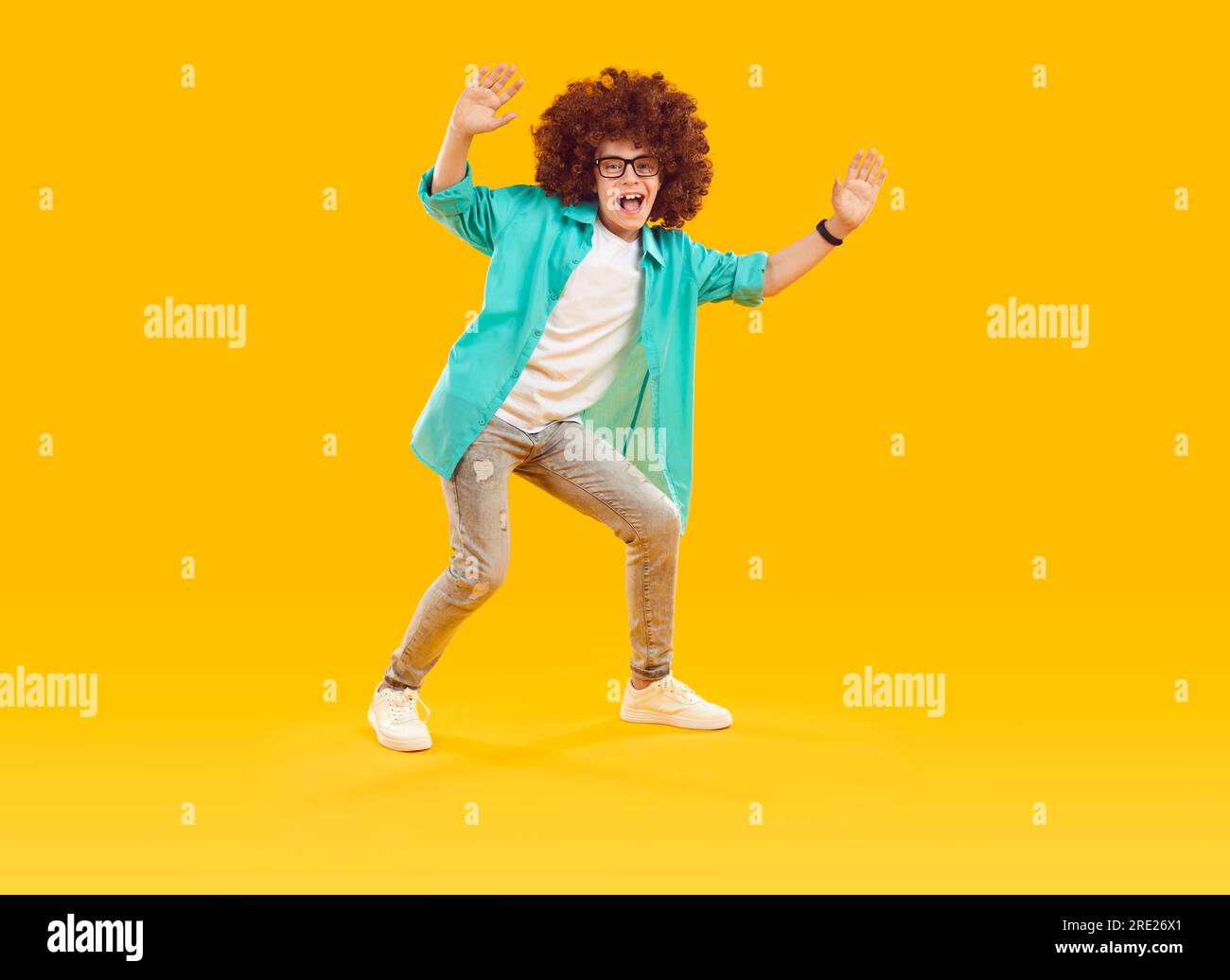 Happy funny joyful little boy in curly wig dancing or waving hello on ...