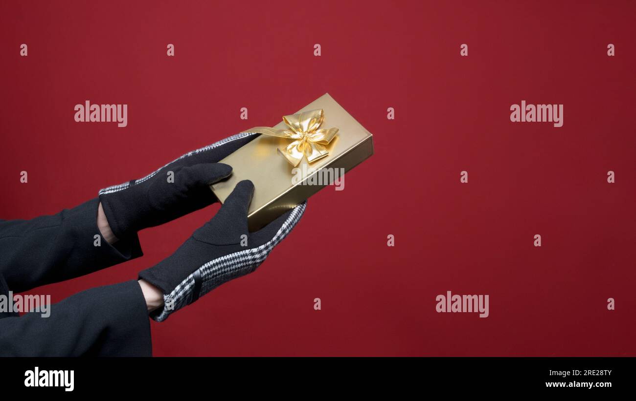 Female hands in elegant gloves hold a gift box with a bow in gold ...