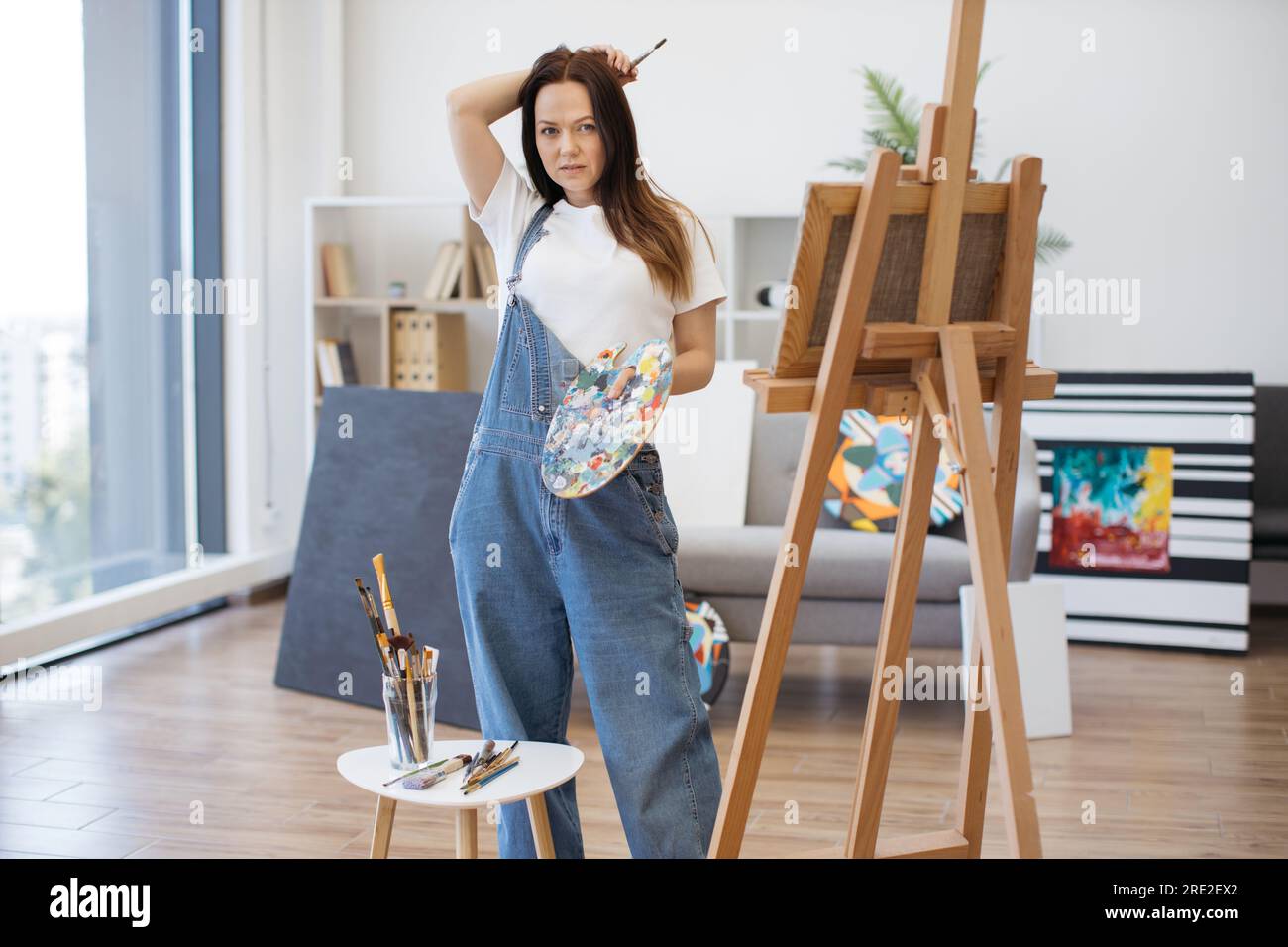 Portrait of beautiful woman in denim overalls posing among artist ...