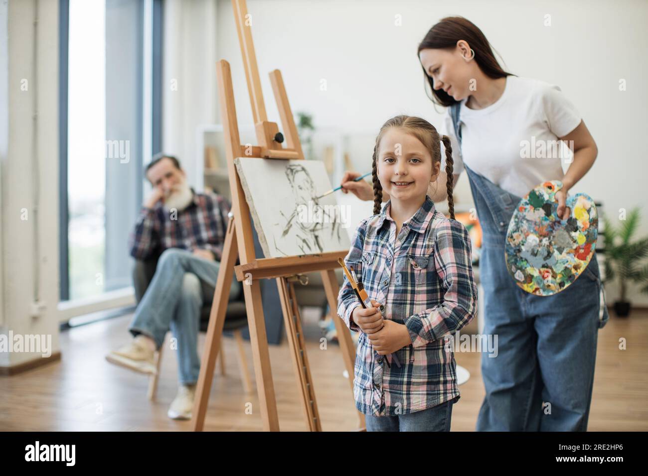 Beautiful girl with paintbrushes looking at camera while young adult ...