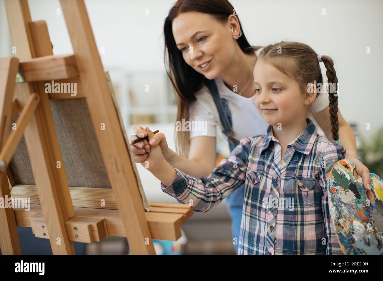 Close up view of involved woman and cute girl applying paint on canvas ...