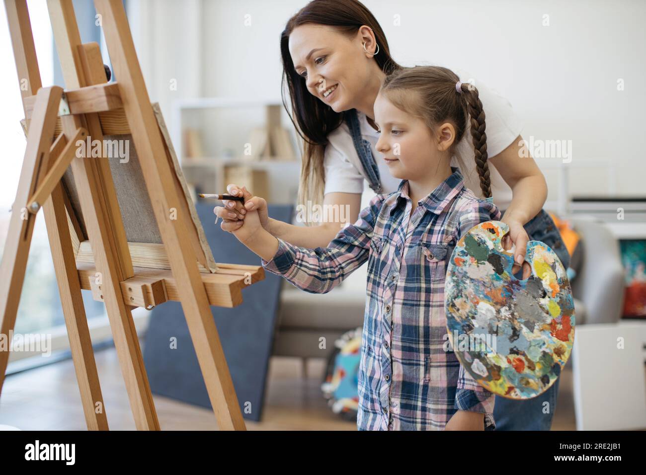 Close up view of involved woman and cute girl applying paint on canvas ...