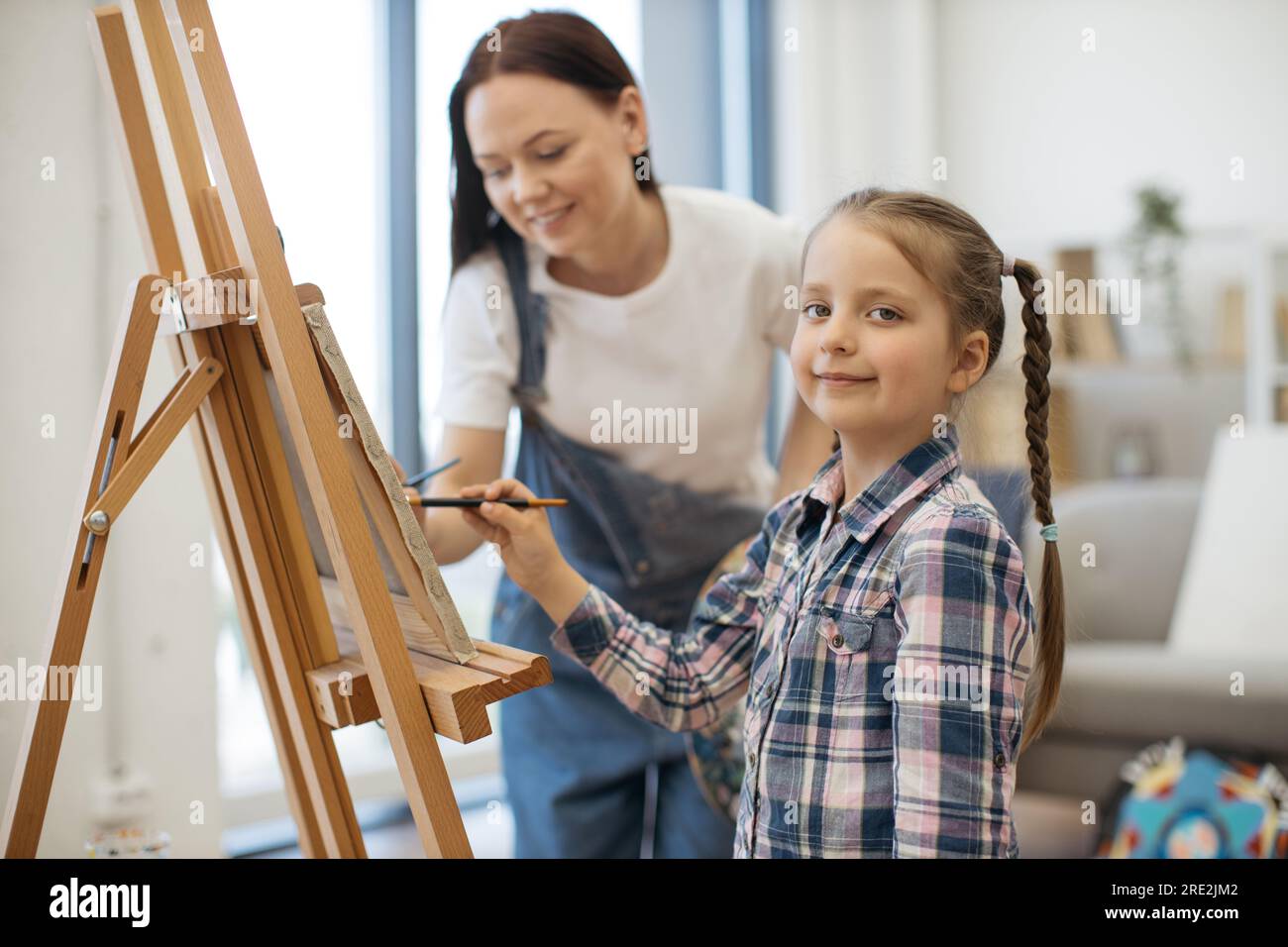 Close up view of involved woman and cute girl applying paint on canvas ...