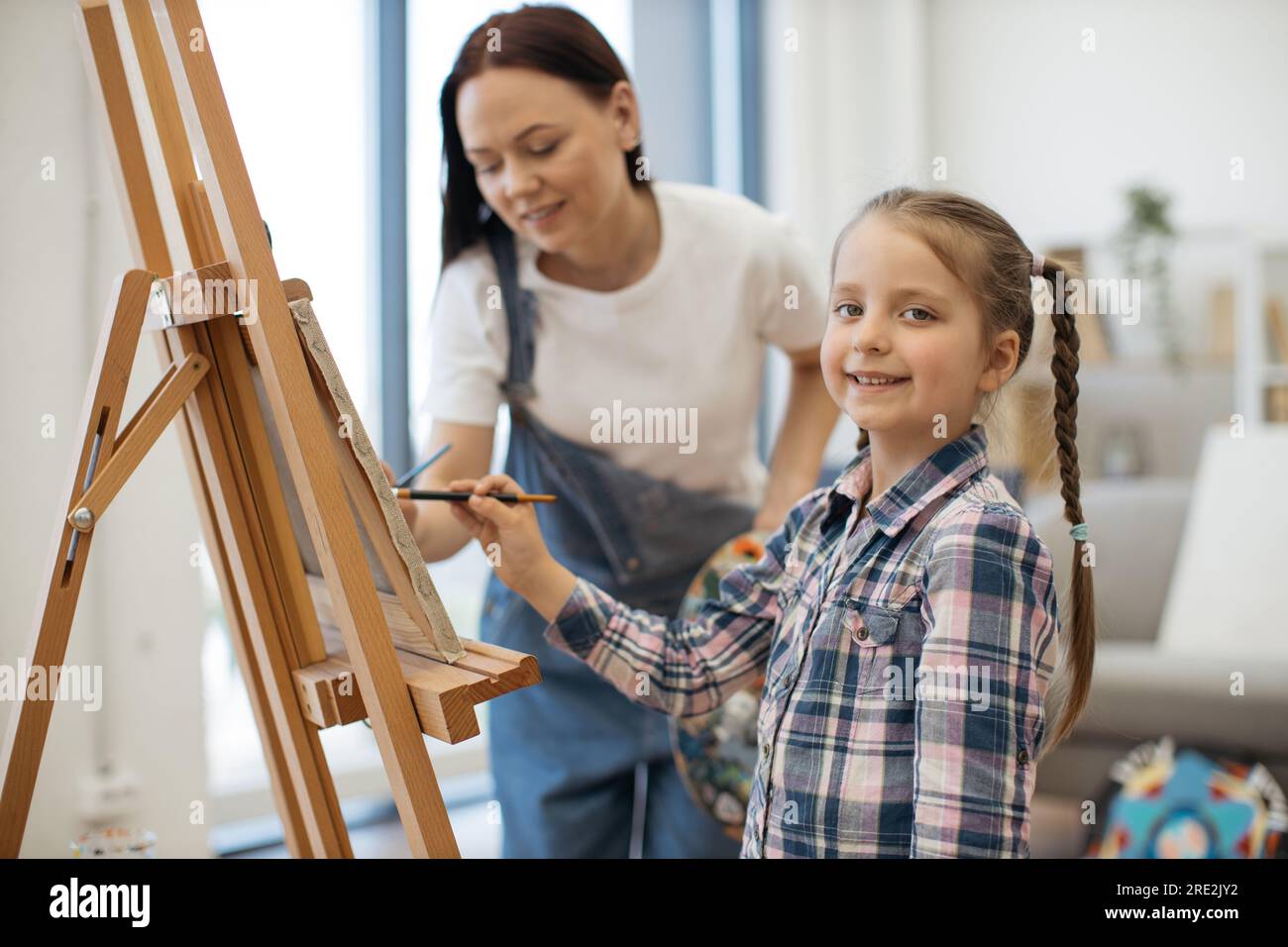Close up view of involved woman and cute girl applying paint on canvas ...