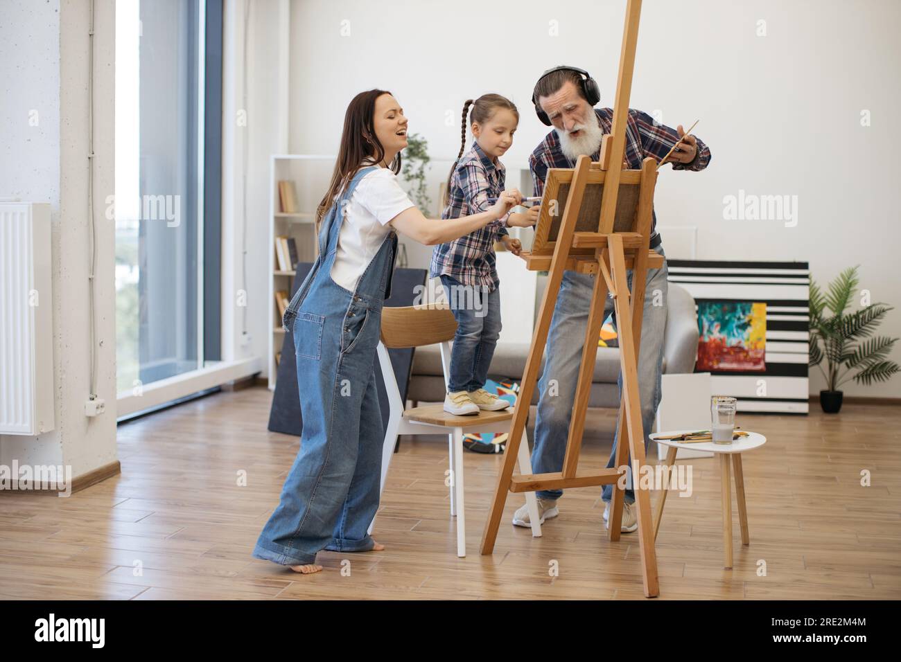 Excited senior man and young females with devices and paintbrushes ...
