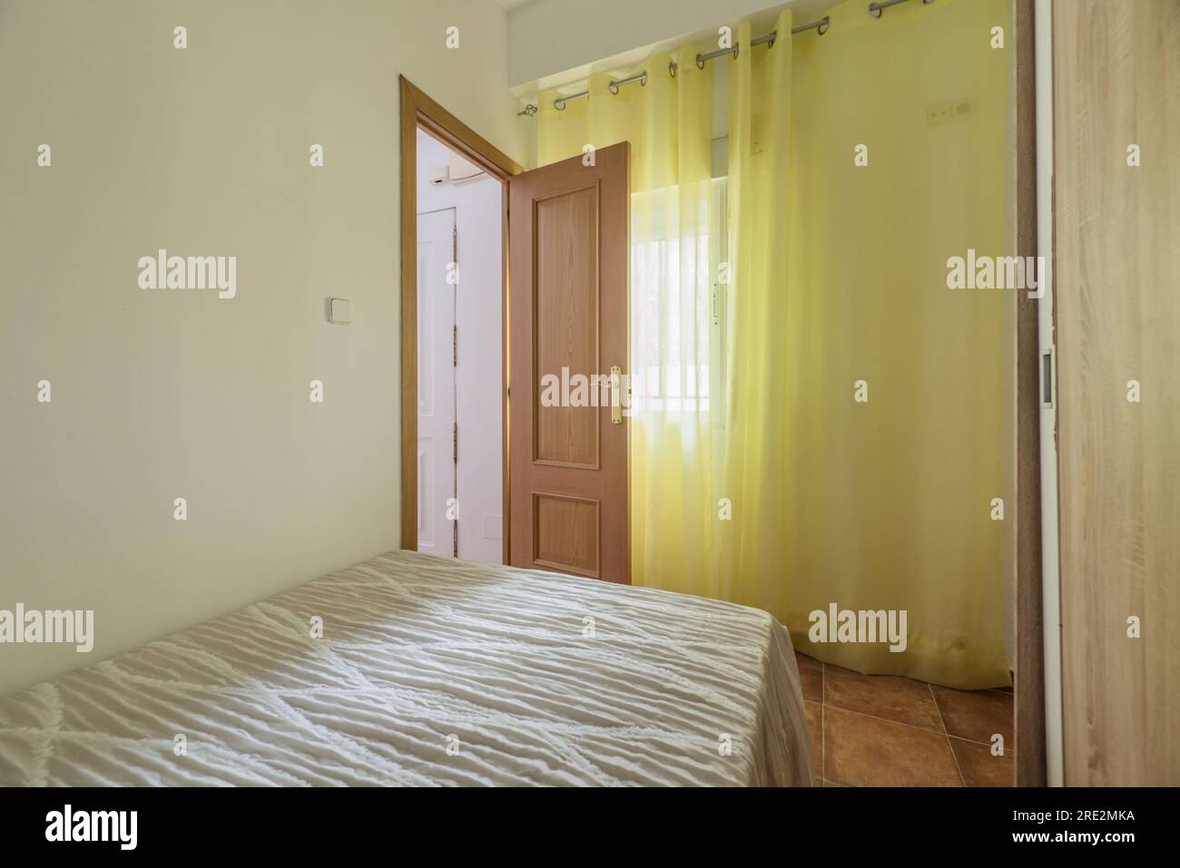 Bedroom with a double bed with a white bedspread, brown stoneware floor ...