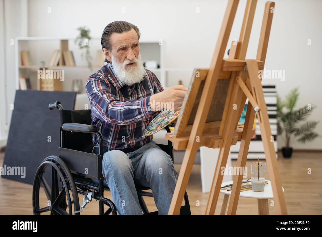Grey-bearded retired man with disability sitting in front of wooden ...