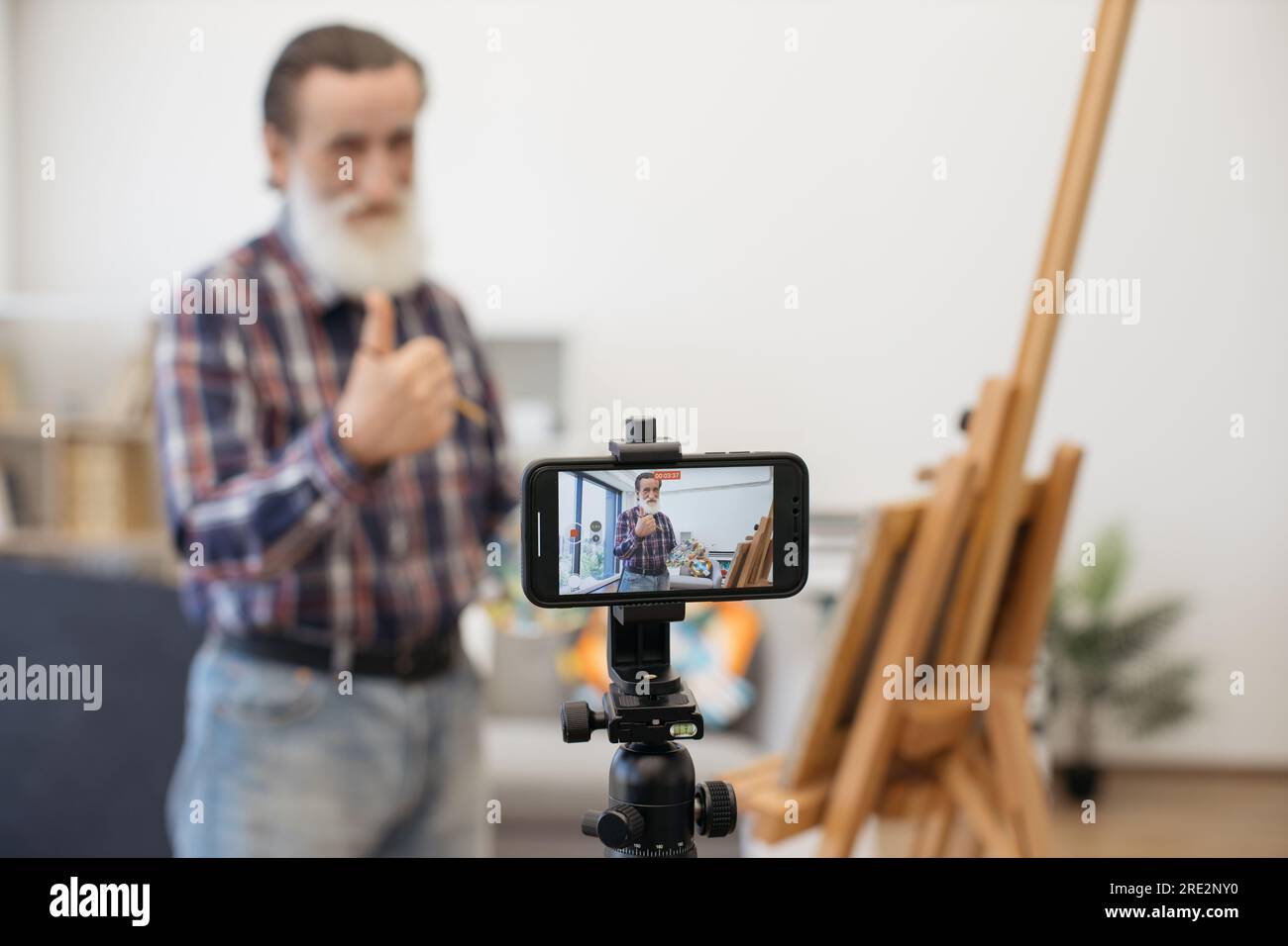 Progressive grey-bearded man using tripod for making selfie on personal ...