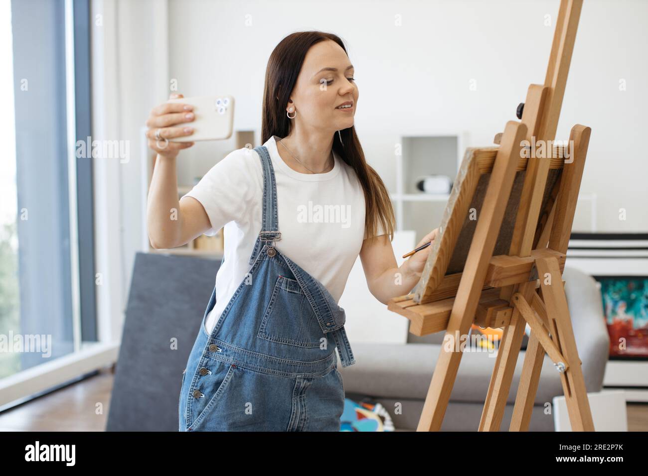 Positive lady in every day clothes making selfie on modern smartphone and waving hand near ...