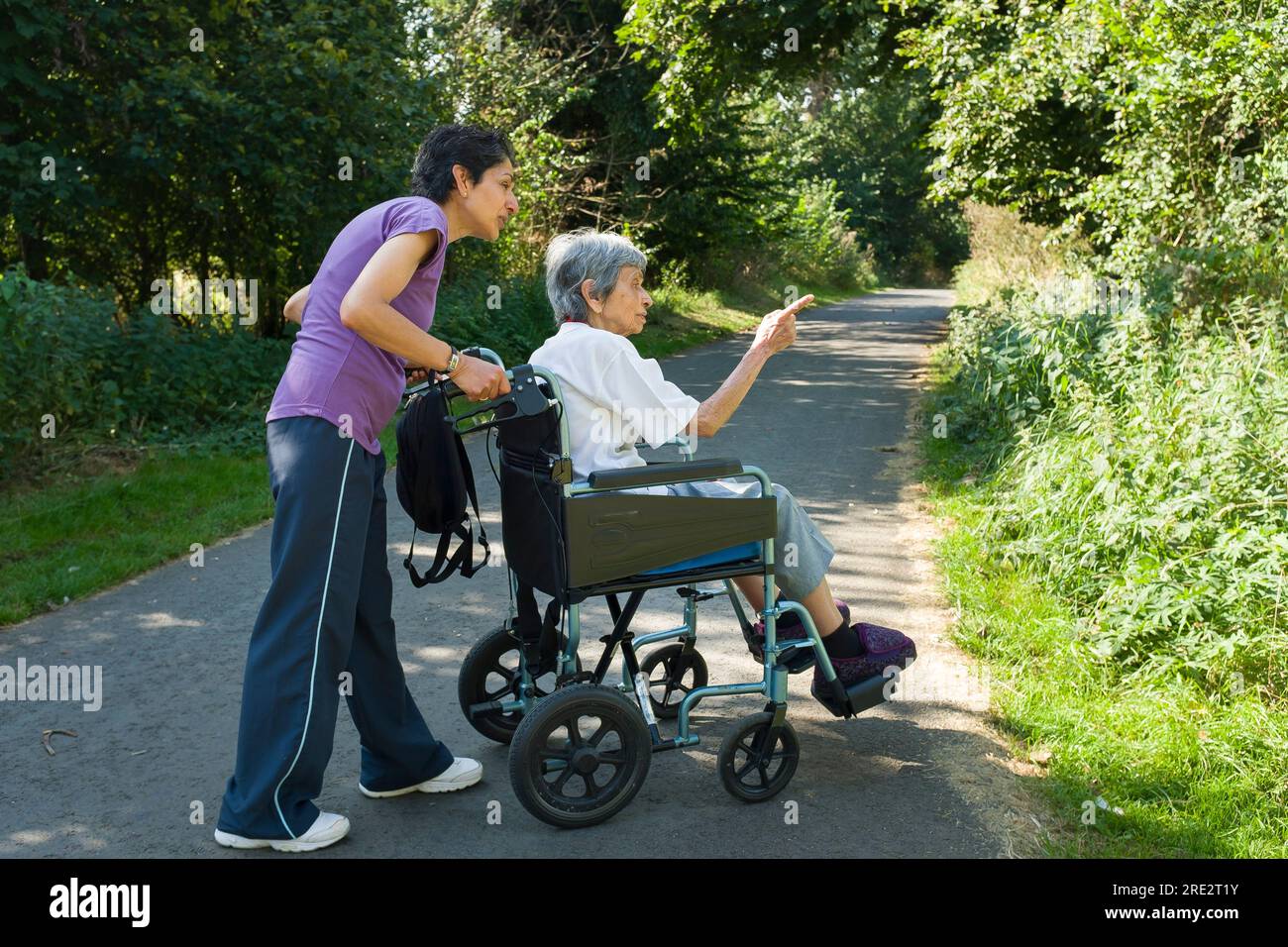 Asian Indian woman pushing her elderly mother in a wheelchair outdoors ...