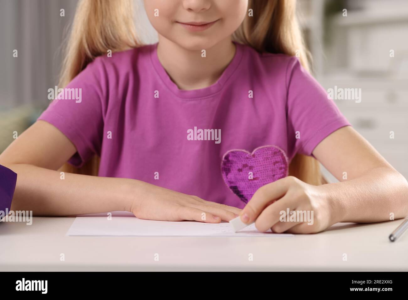 Girl erasing mistake in her homework at white desk in room, closeup ...