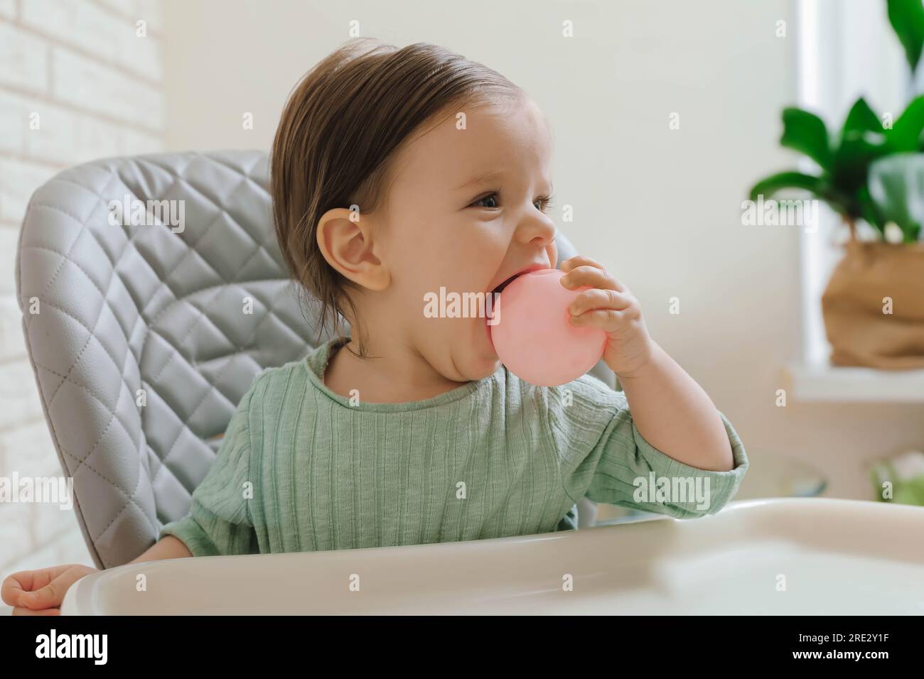 Cute little baby nibbling toy in high chair indoors Stock Photo - Alamy