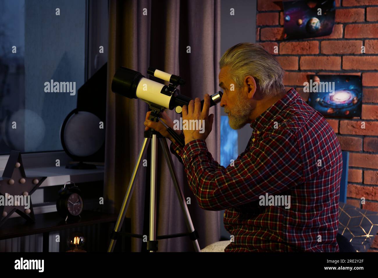 Senior man looking at stars through telescope in room Stock Photo - Alamy