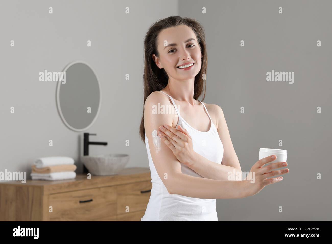 Happy woman applying body cream onto arm in bathroom, space for text ...