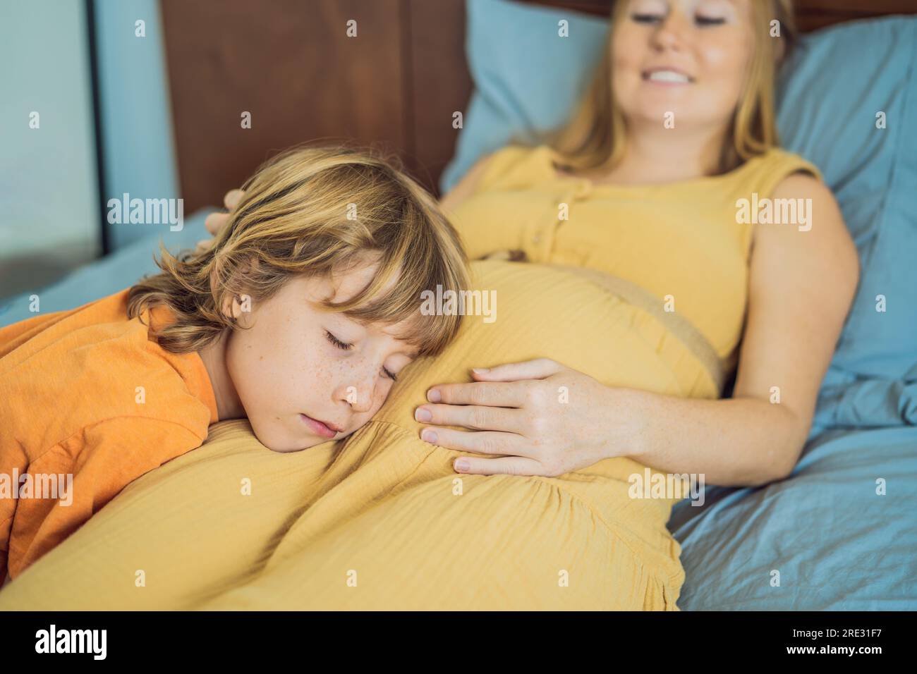 Young pregnant mother hugging her little boy lying in bed at night ...