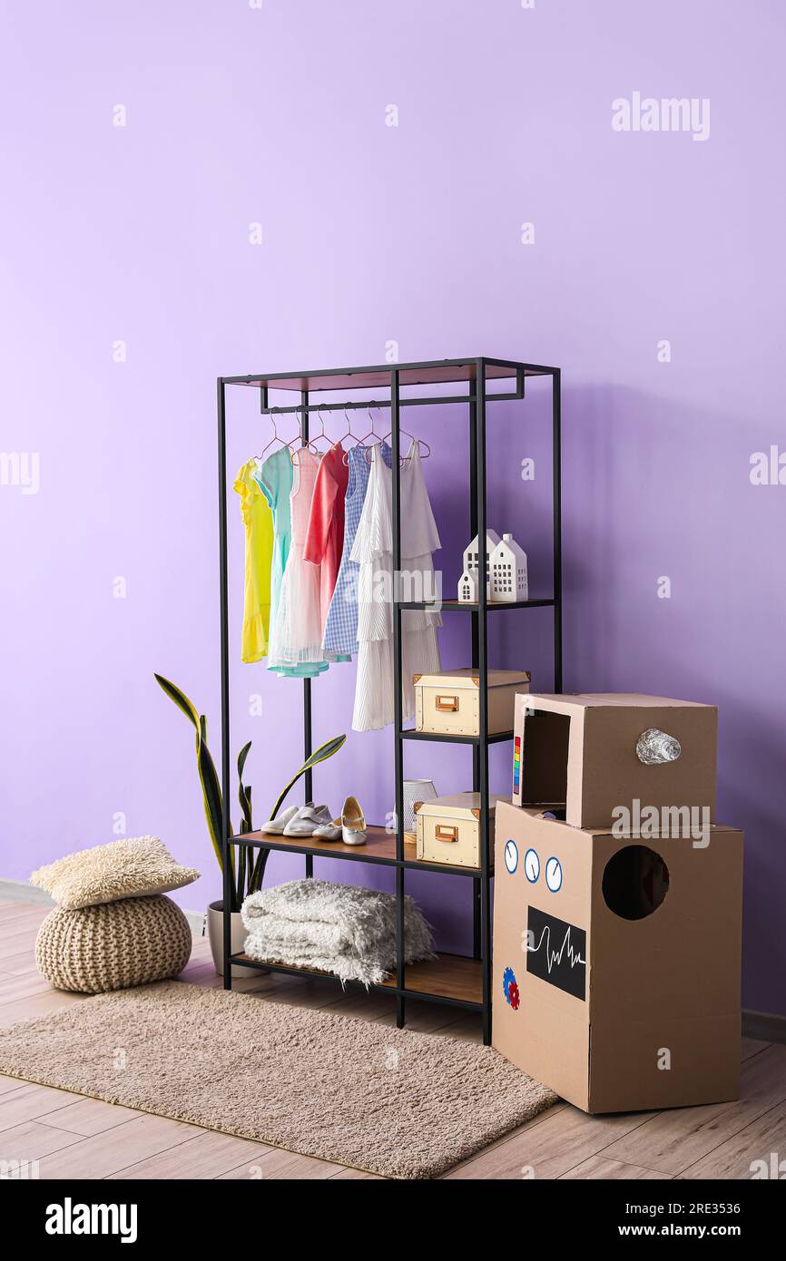 Shelving unit with children's dresses and shoes near lilac wall in room ...
