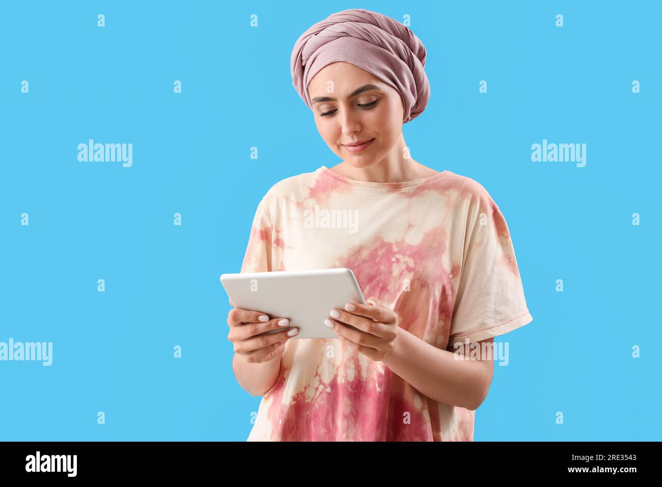 Young woman after chemotherapy with tablet computer on blue background ...