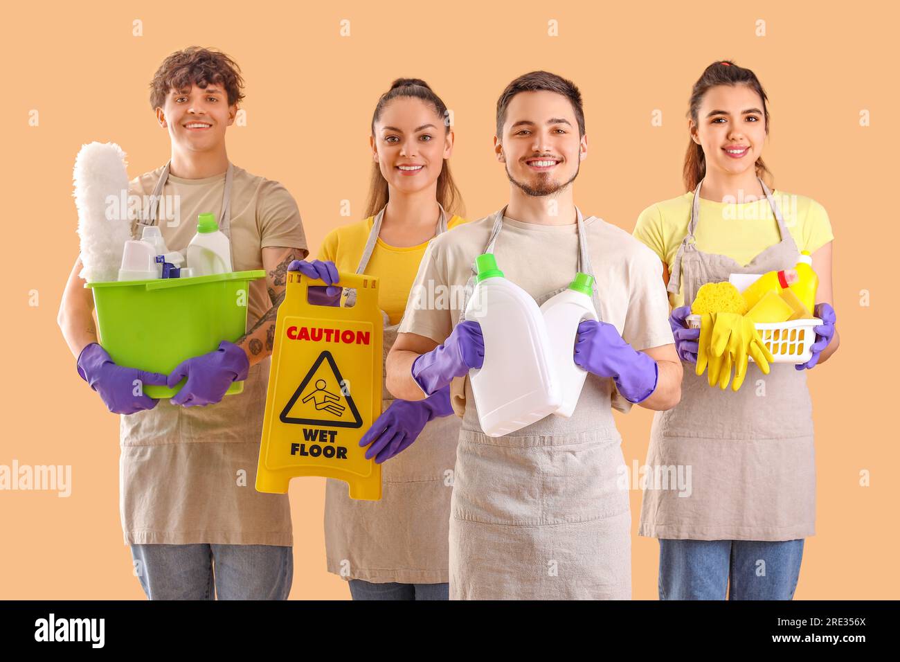 Young janitors with cleaning supplies on beige background Stock Photo ...