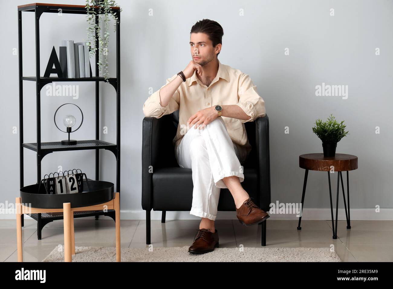 Stylish young man with wristwatch sitting on armchair in room Stock ...