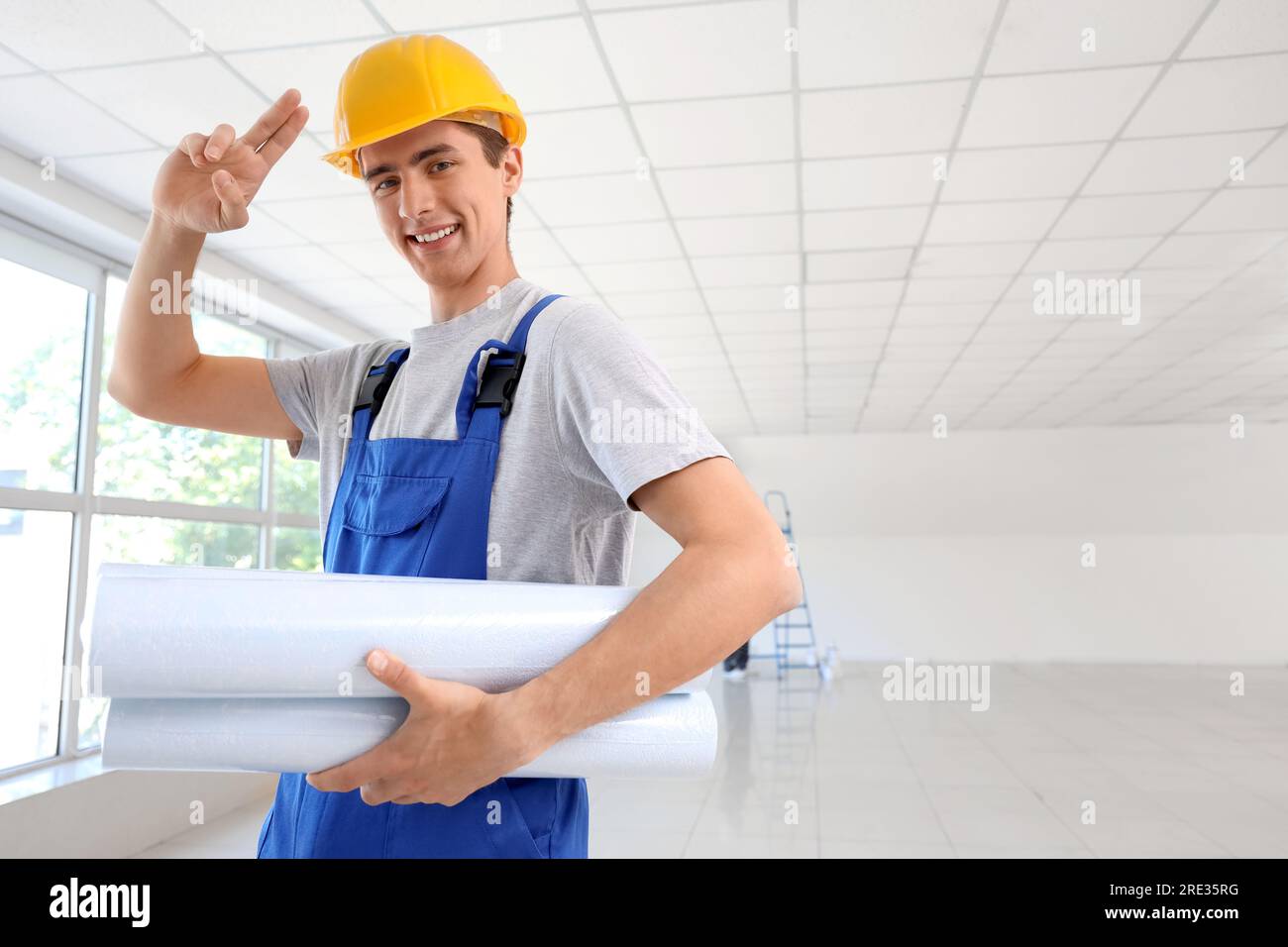 Male builder with wallpapers saluting in room Stock Photo - Alamy