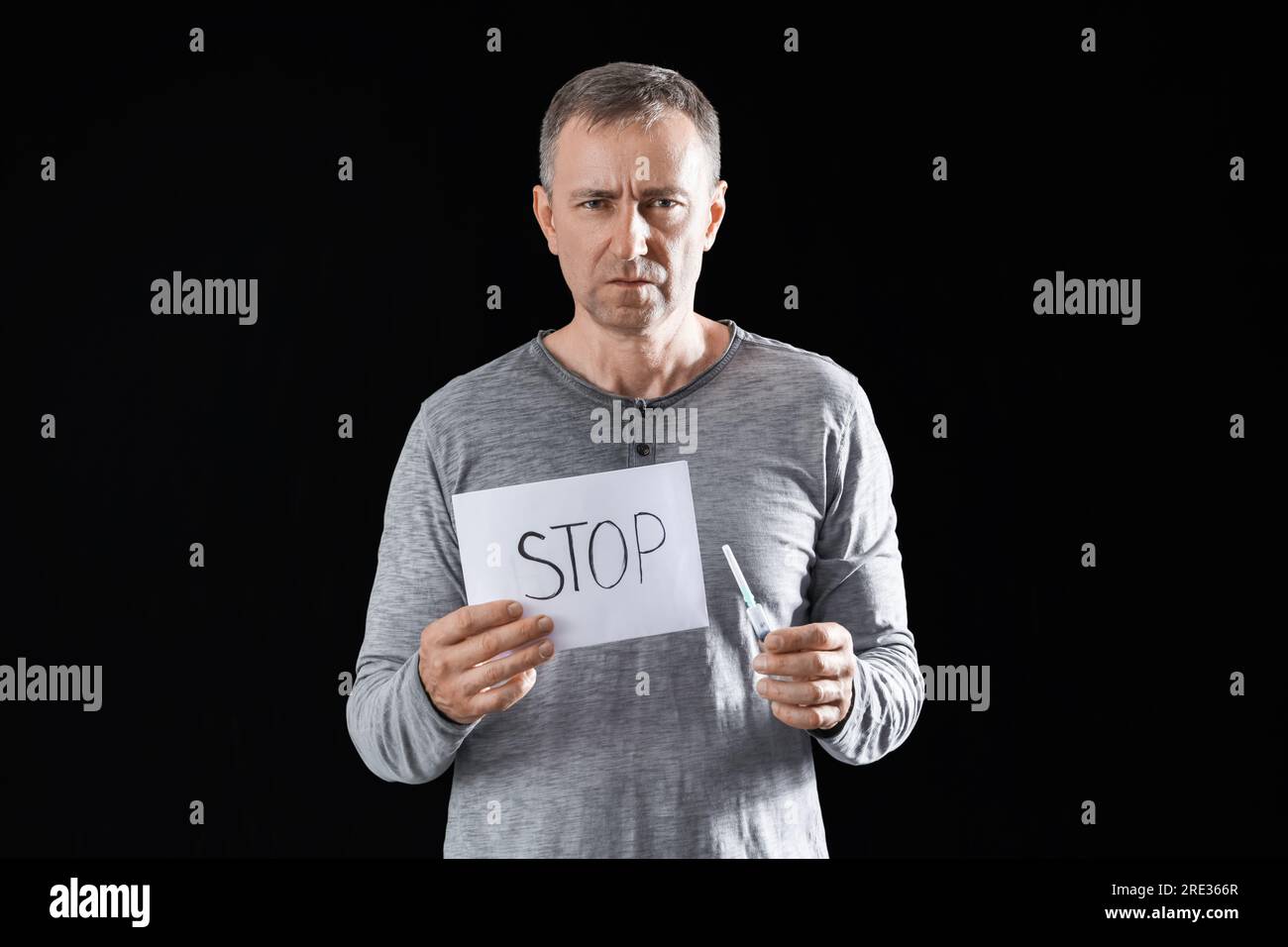 Mature drug addict holding paper with word STOP and syringe on black ...