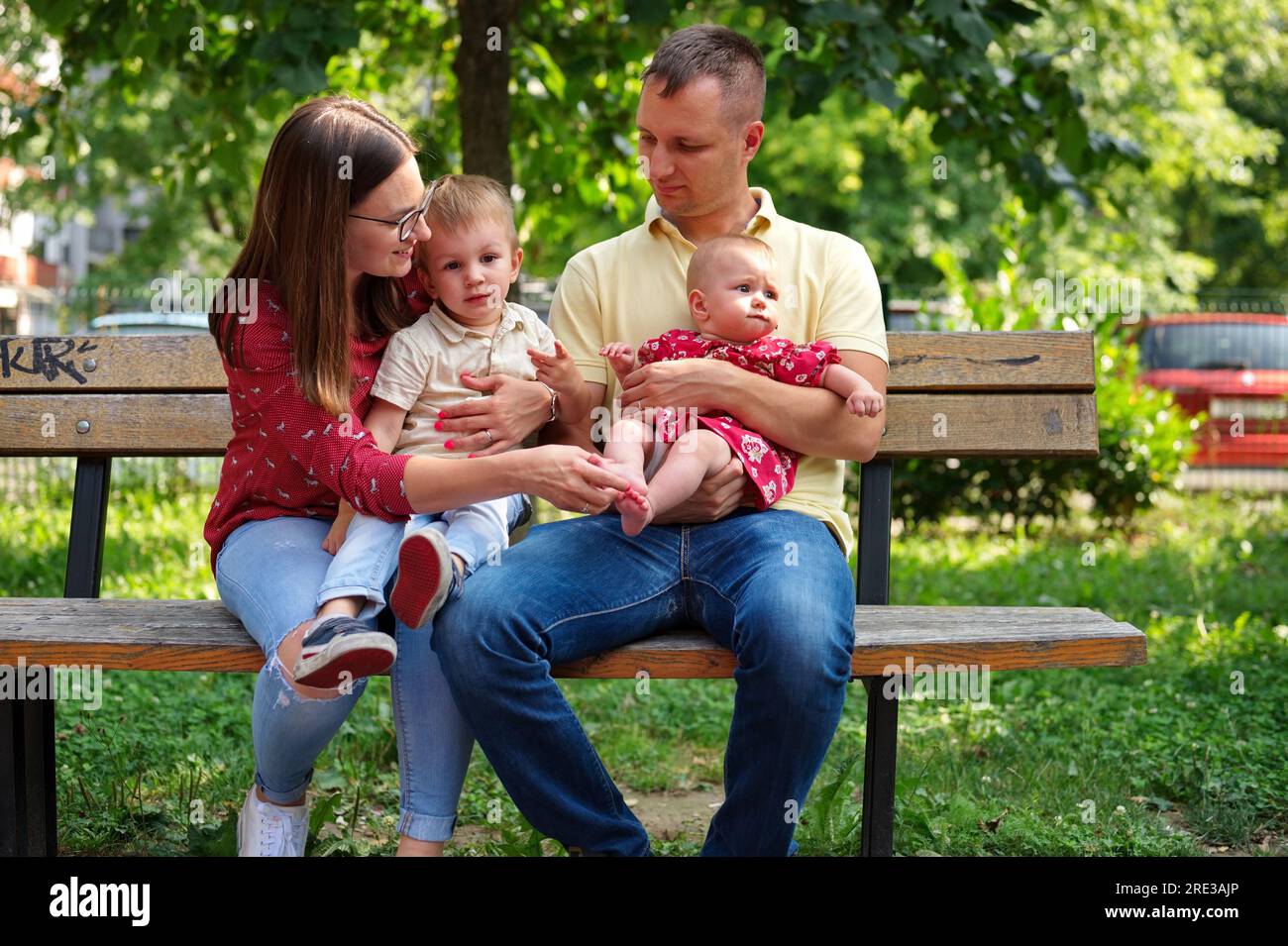 Family with two children sitting on a bench in the park Stock Photo - Alamy