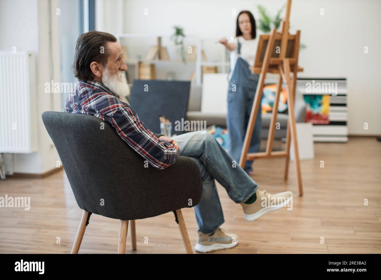 Focus on senior man in stylish wear sitting in soft chair while young ...