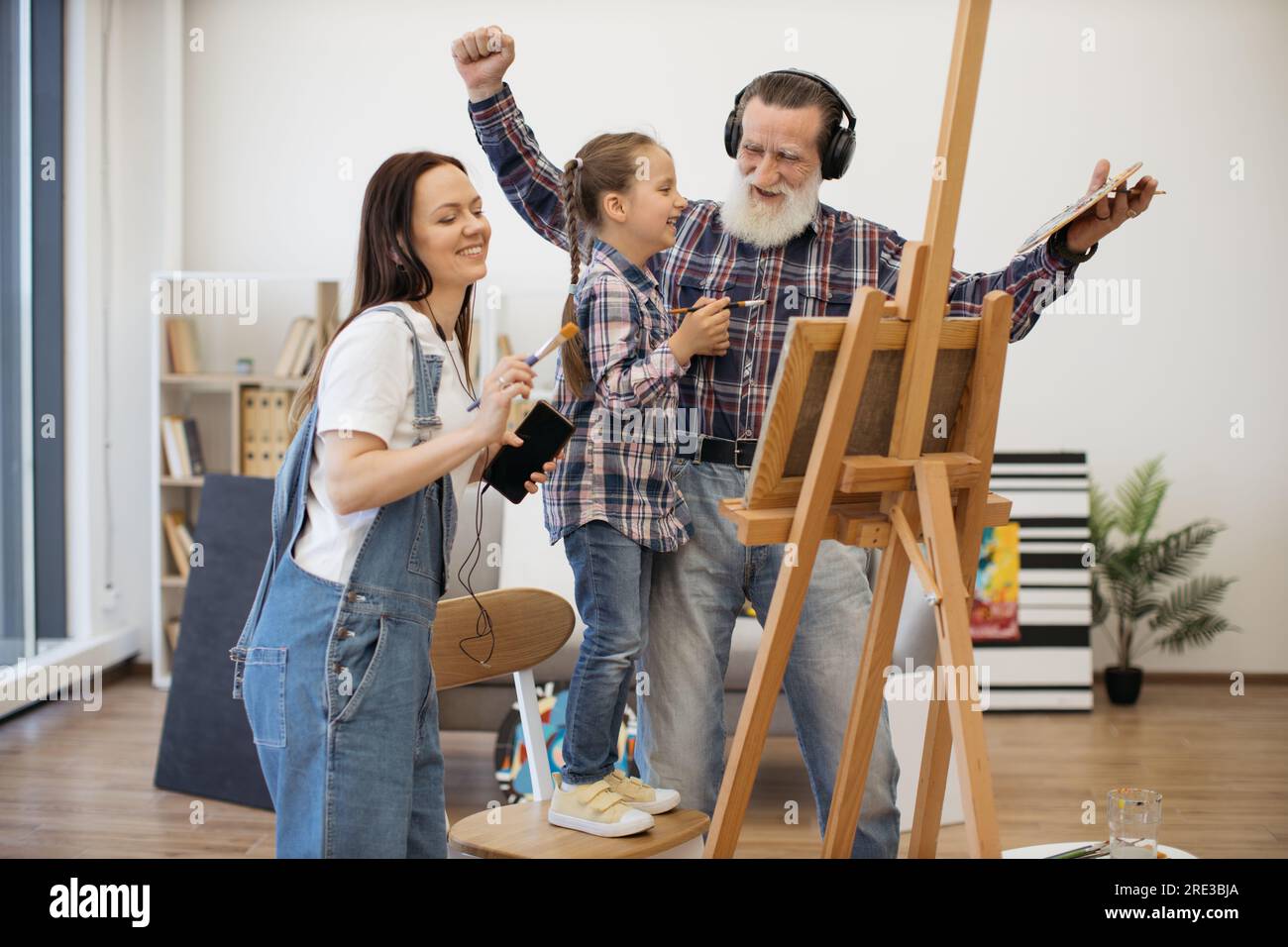 Relaxed woman with earbuds making collage on canvas with happy daughter ...