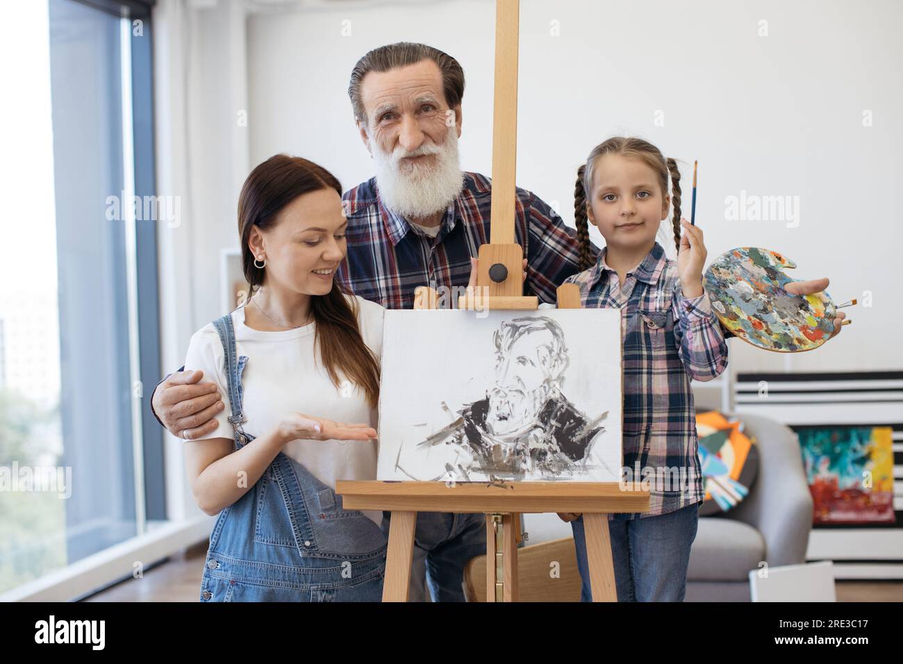 Artists family embracing together near easel with picture at bright art ...