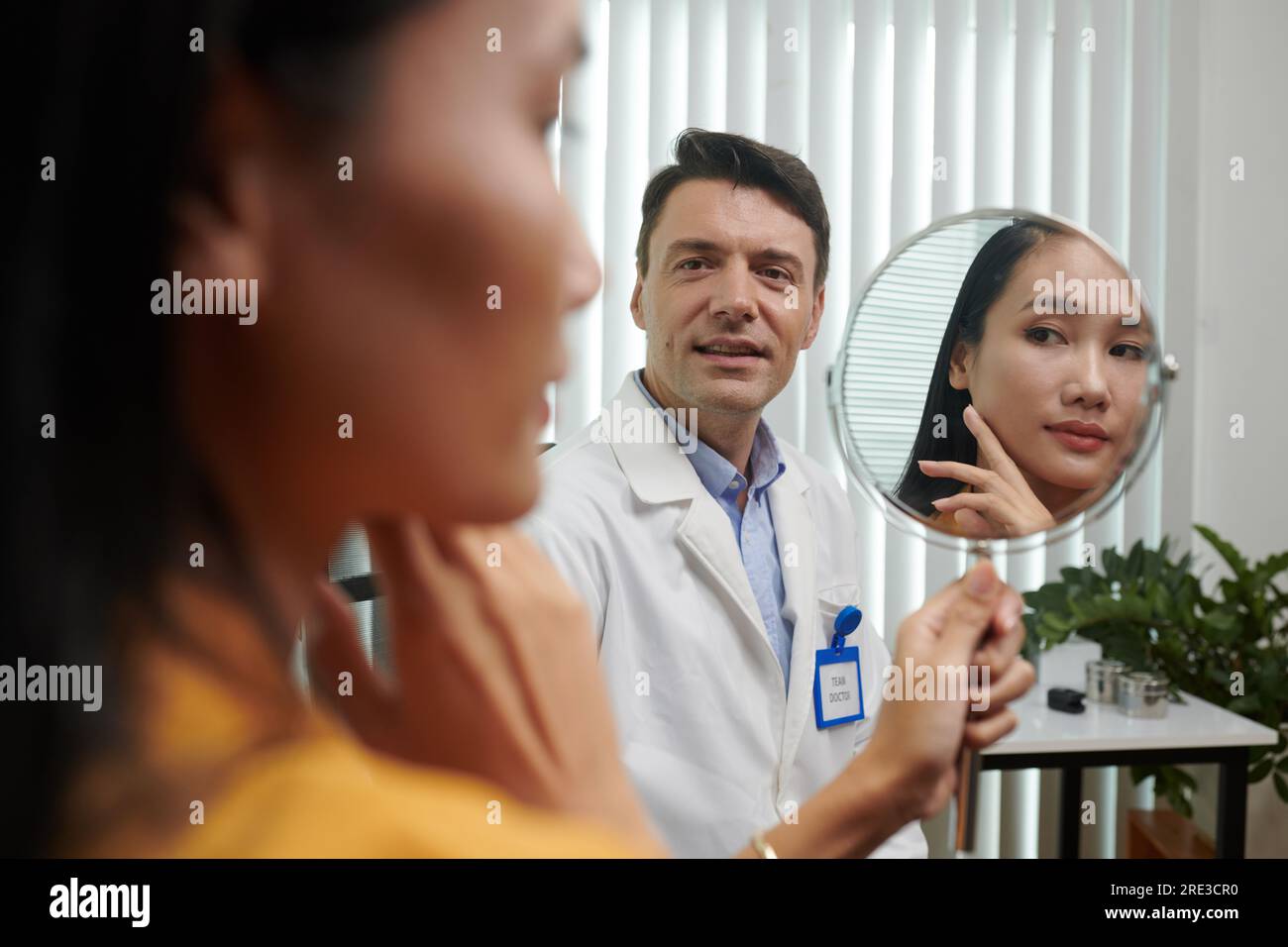 Plastic surgeon giving mirror to patient, letting her look at her new ...