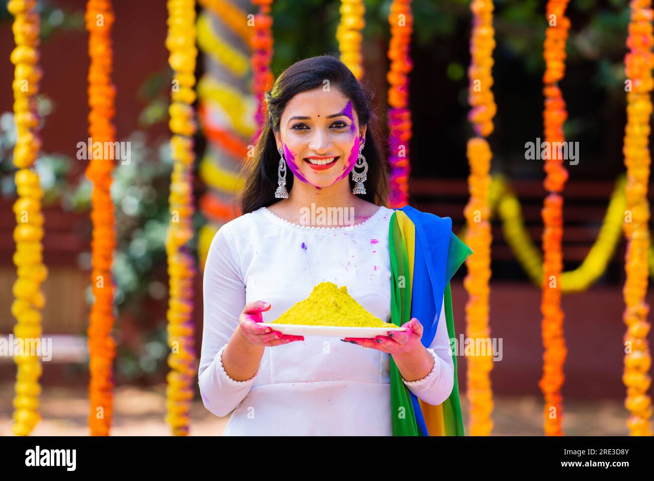 Happy smiling girl with holi color on face by holding holi powder plate ...
