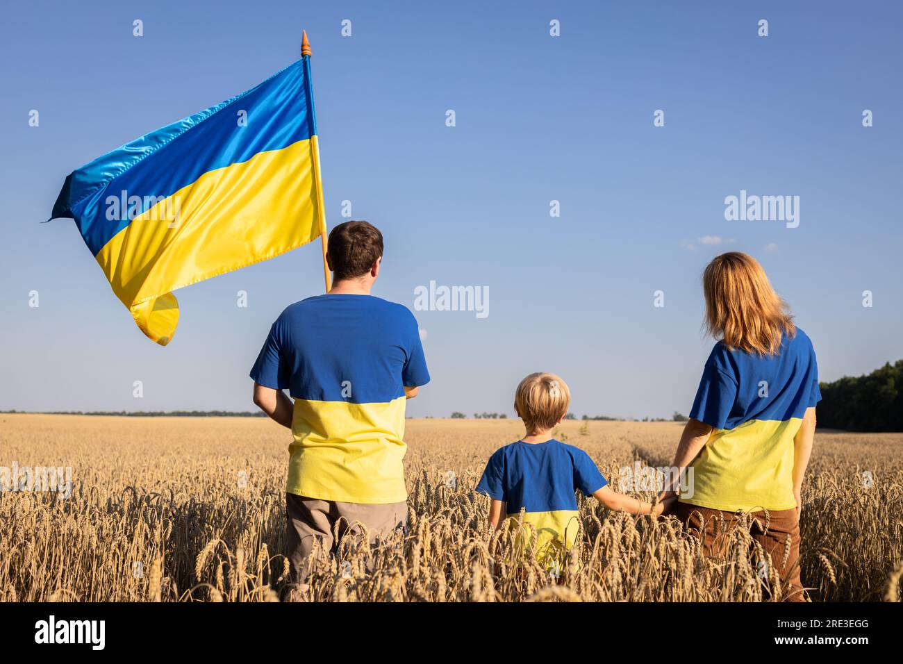 Ukrainian family in yellow-blue t-shirts and flag of Ukraine stands ...