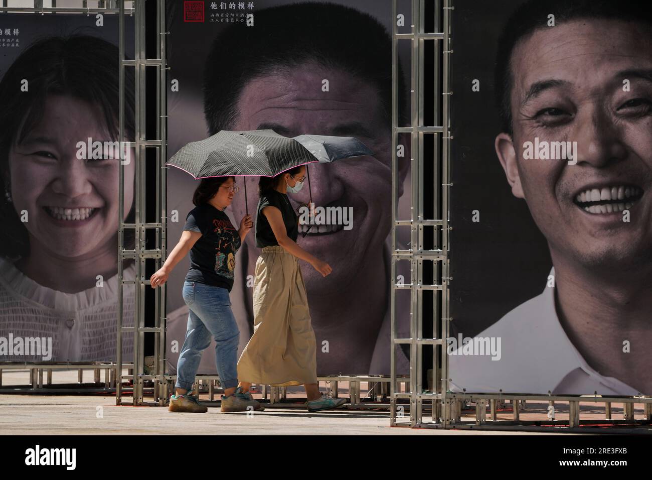 Women carrying umbrellas walk by frames displaying portraits of workers ...