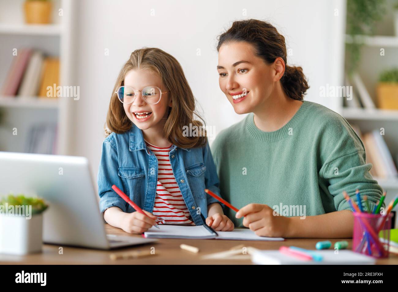Happy child and adult are sitting at desk. Girl doing homework or ...