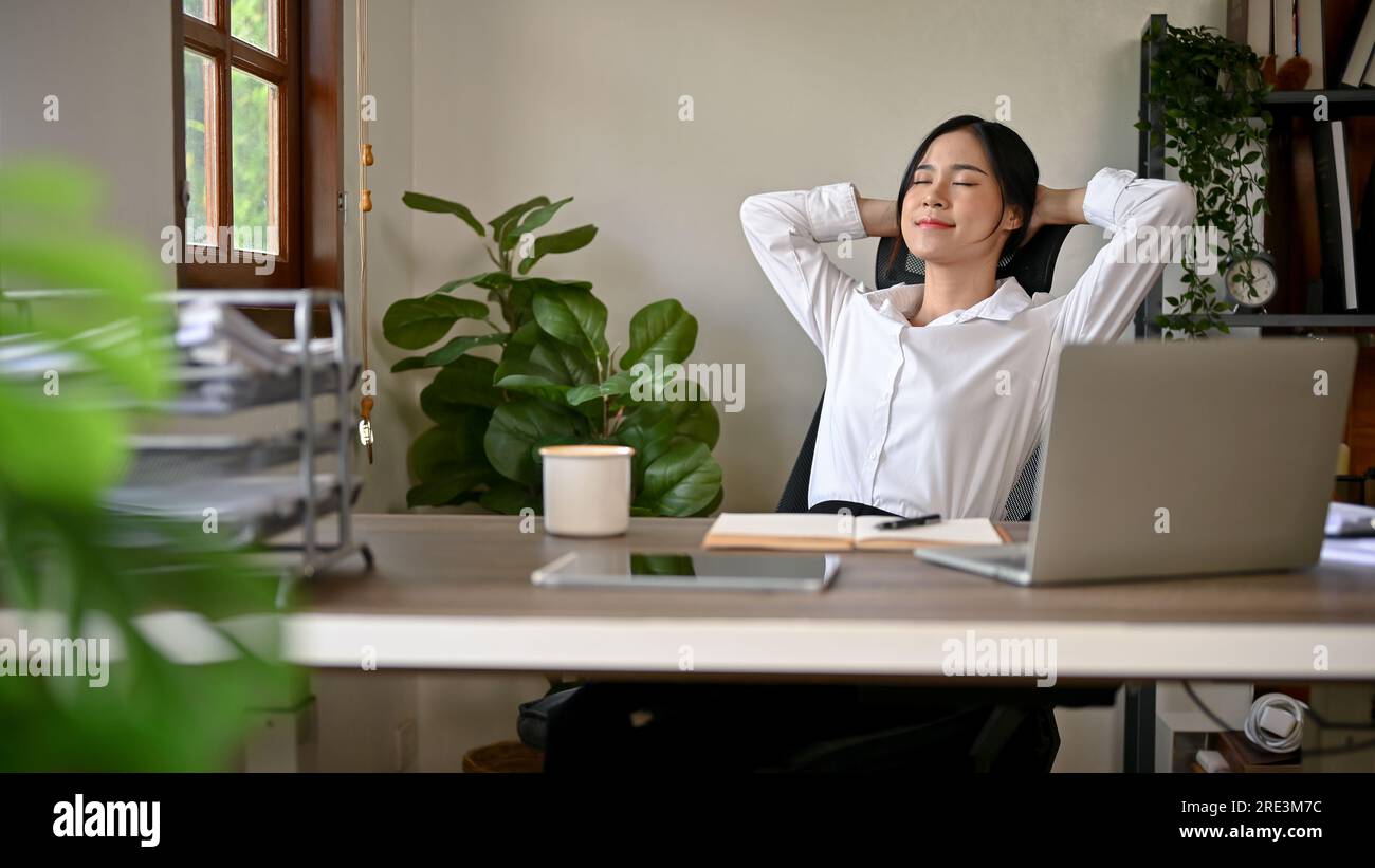 A happy and relaxed Asian businesswoman is leaning on her chair ...