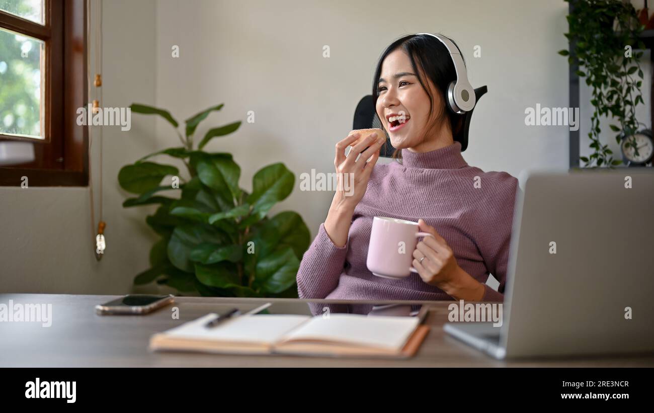 Beautiful young Asian girl eating a donut while studying at her study ...