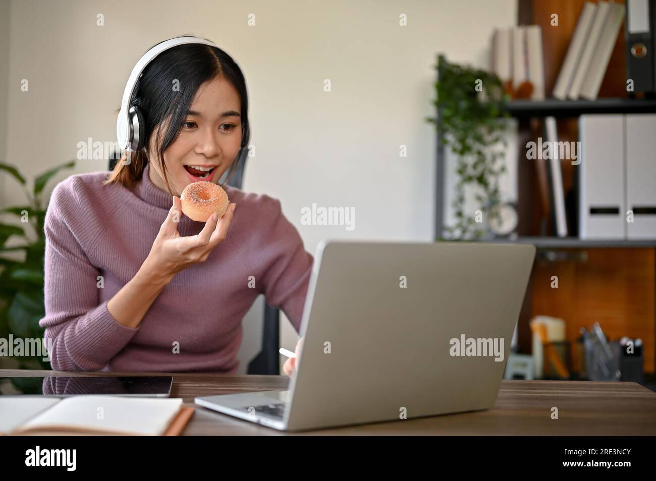 Beautiful young Asian girl eating a donut while studying at her study ...