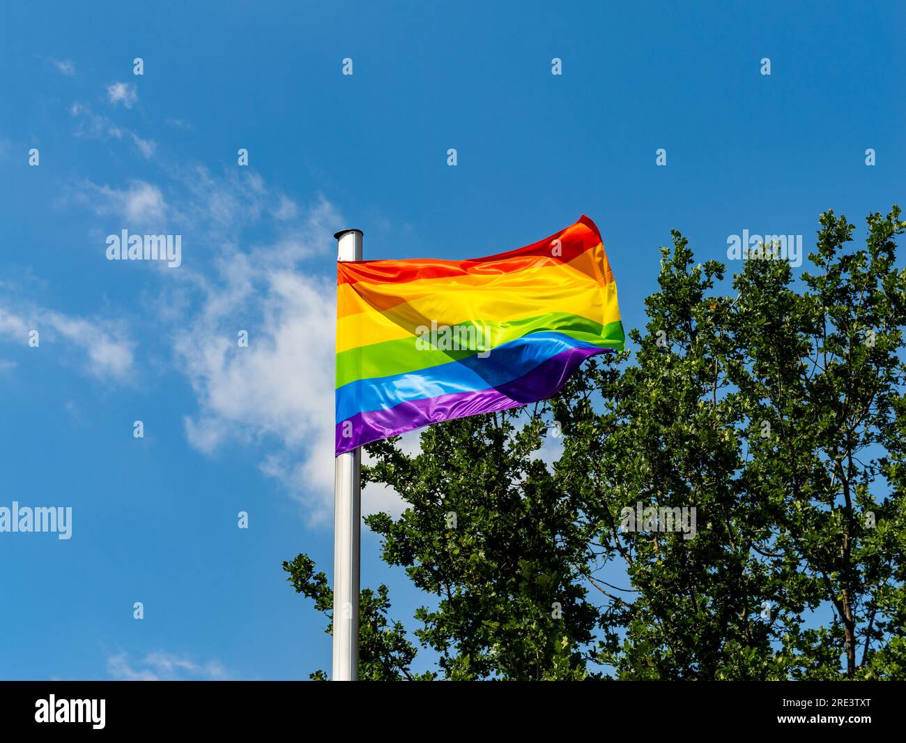 Rainbow flag (LGBT pride) fluttering in the wind in front of a blue sky ...