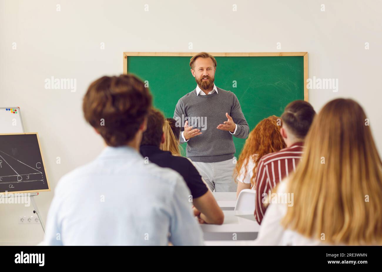 Math teacher standing in classroom and talking to group of school or ...